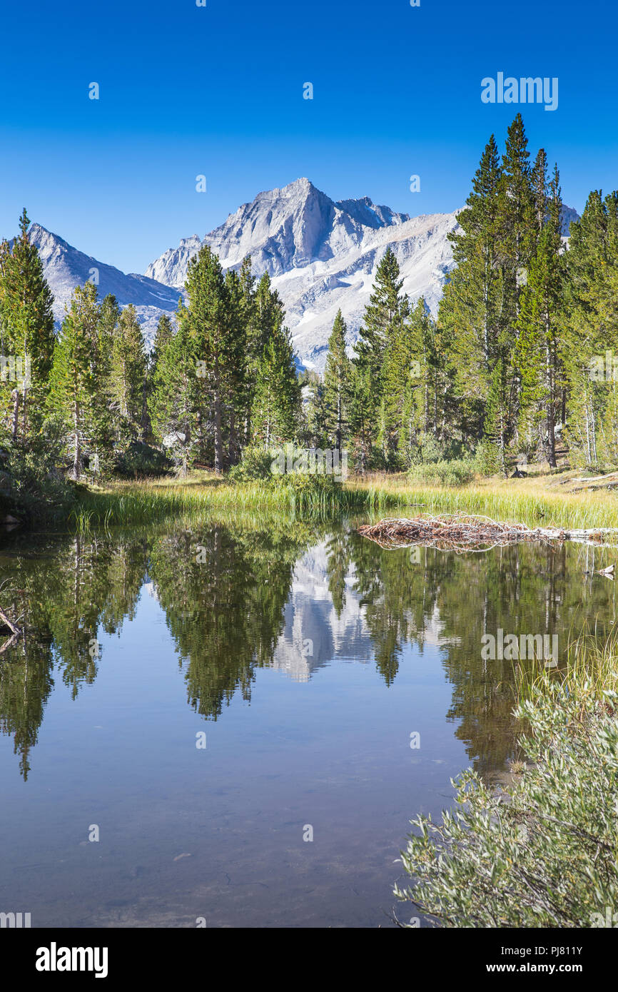 A small unnamed mountain lake reflects the distant mountain peaks and ...
