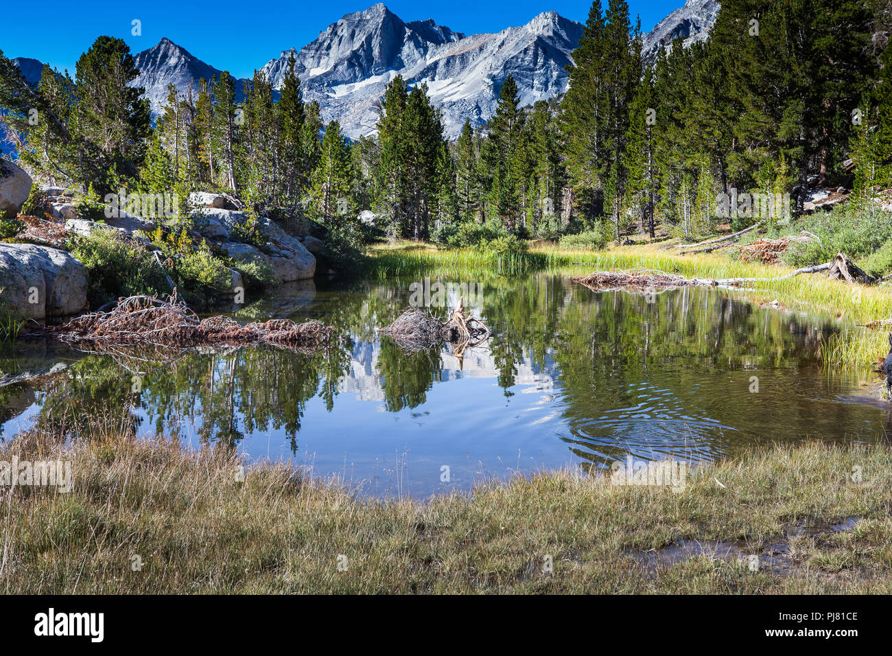 A small unnamed mountain lake reflects the distant mountain peaks and ...