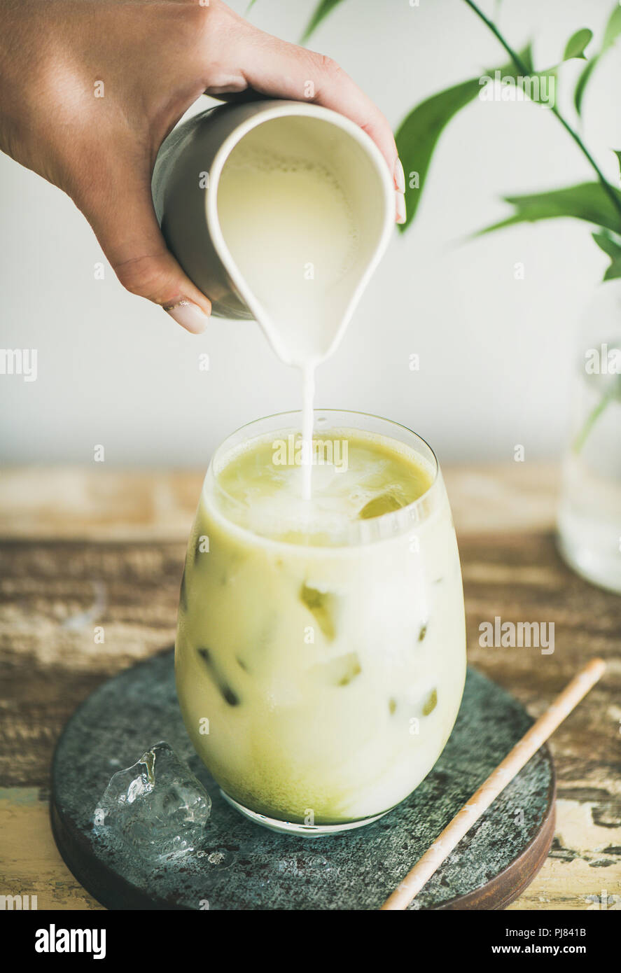 Iced matcha latte drink in glass with coconut milk pouring from pitcher ...