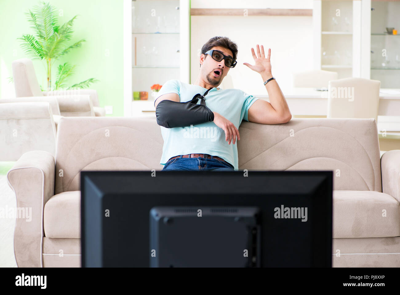 Arm injured man sitting on the sofa watching tv Stock Photo - Alamy
