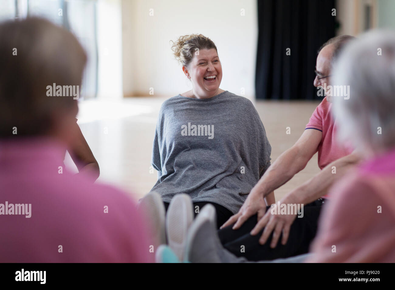 Laughing instructor and active seniors stretching legs in exercise ...