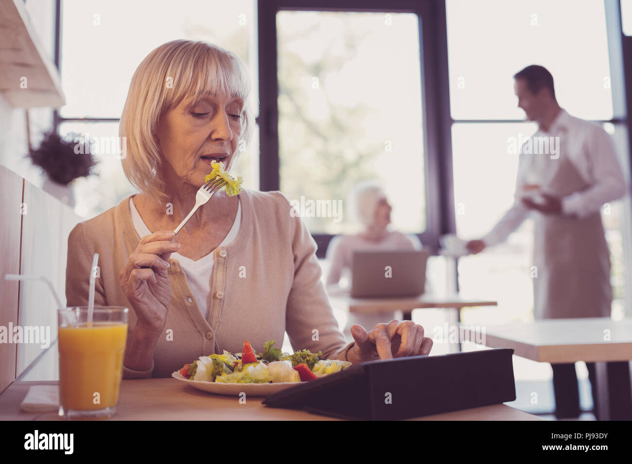 Serious concentrated woman eating and using a tablet Stock Photo - Alamy