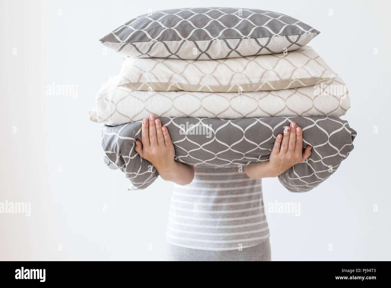 Hands of woman holding modern beige and grey bed linen pile, white wall ...