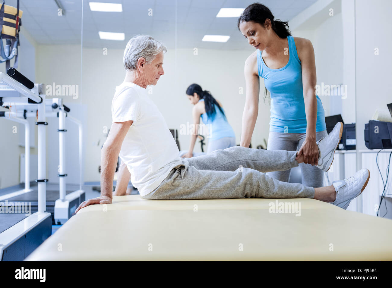 Kind professional trainer warming the injured muscles of her aged ...