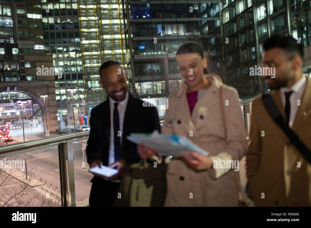 Business people reviewing paperwork on urban pedestrian bridge at night ...