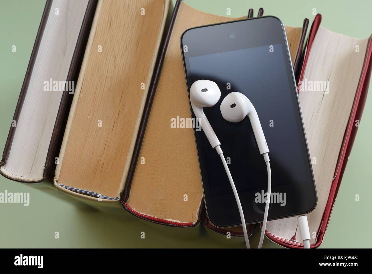 Phone with white earpods on stack of books audiobook storytel podcast ...