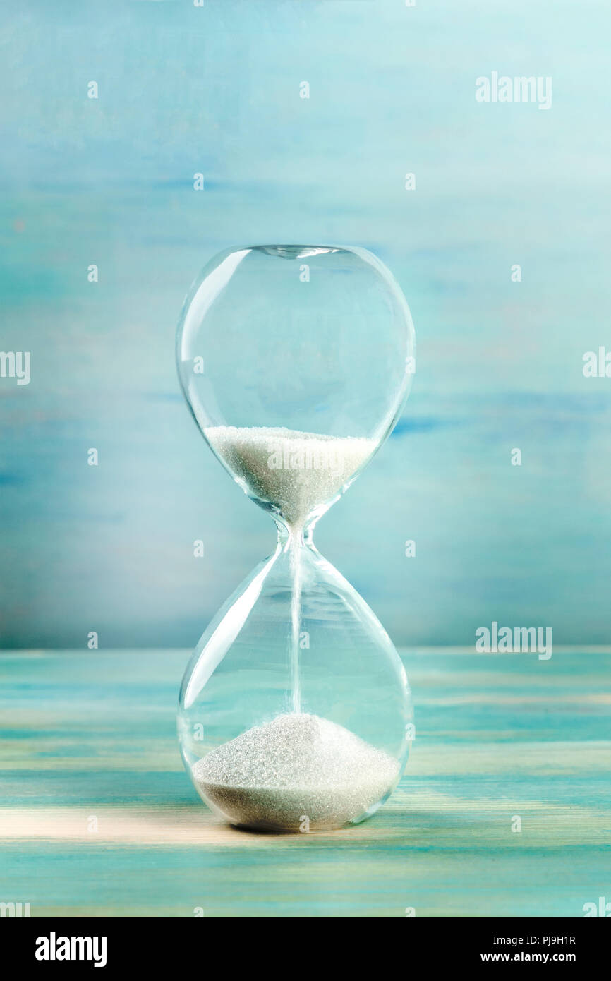 A side view of an hourglass with falling sand, on a teal background ...