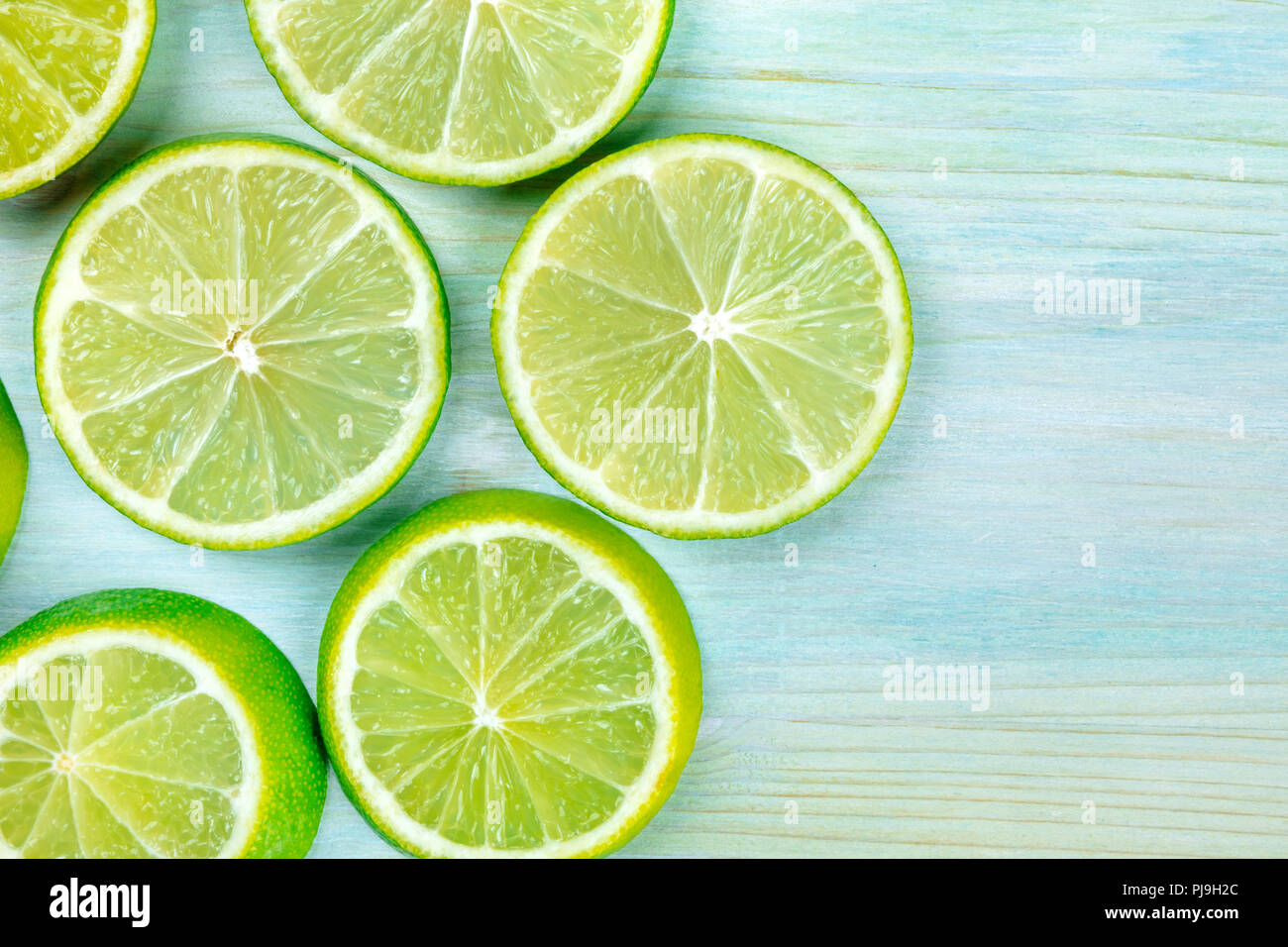 An overhead photo of many vibrant lime slices on a teal blue background ...