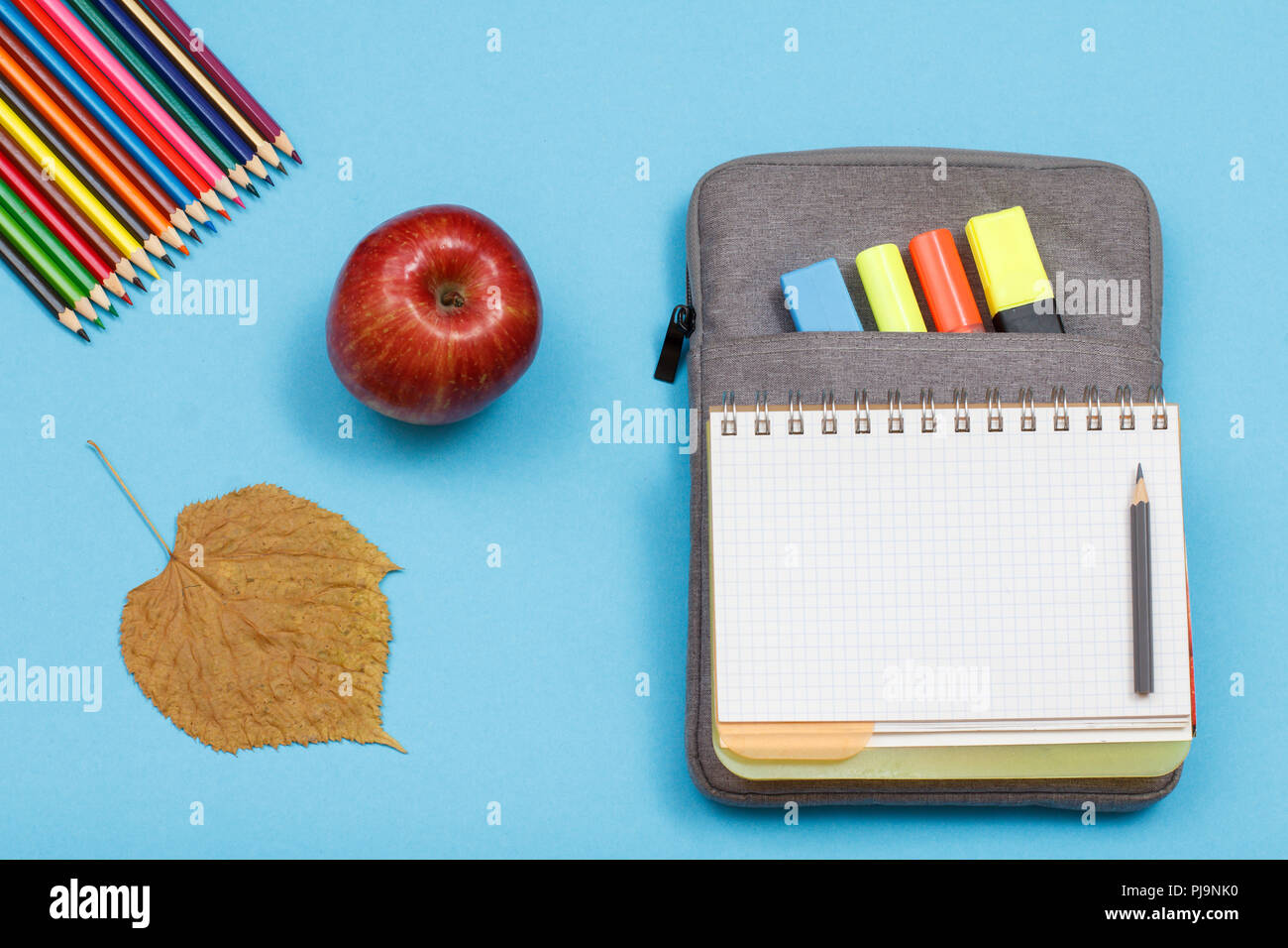 Color pencils, apple, dry leaf, open exercise book on bag-pencil case ...