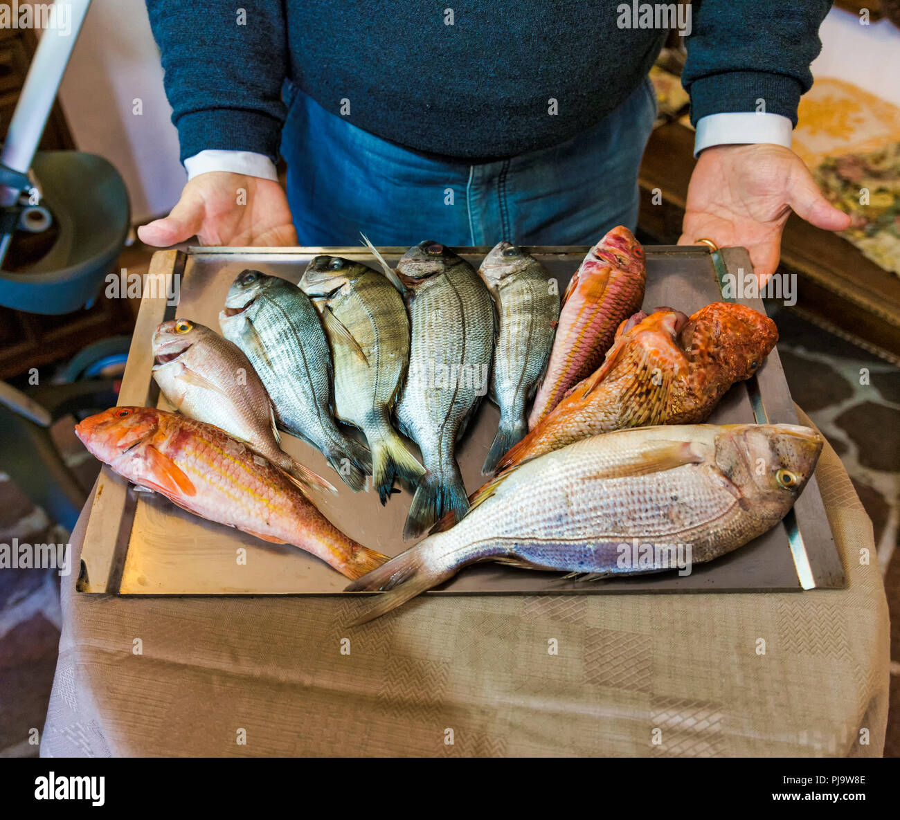 a man in a restaurant presents a plate with various types of fresh fish ...