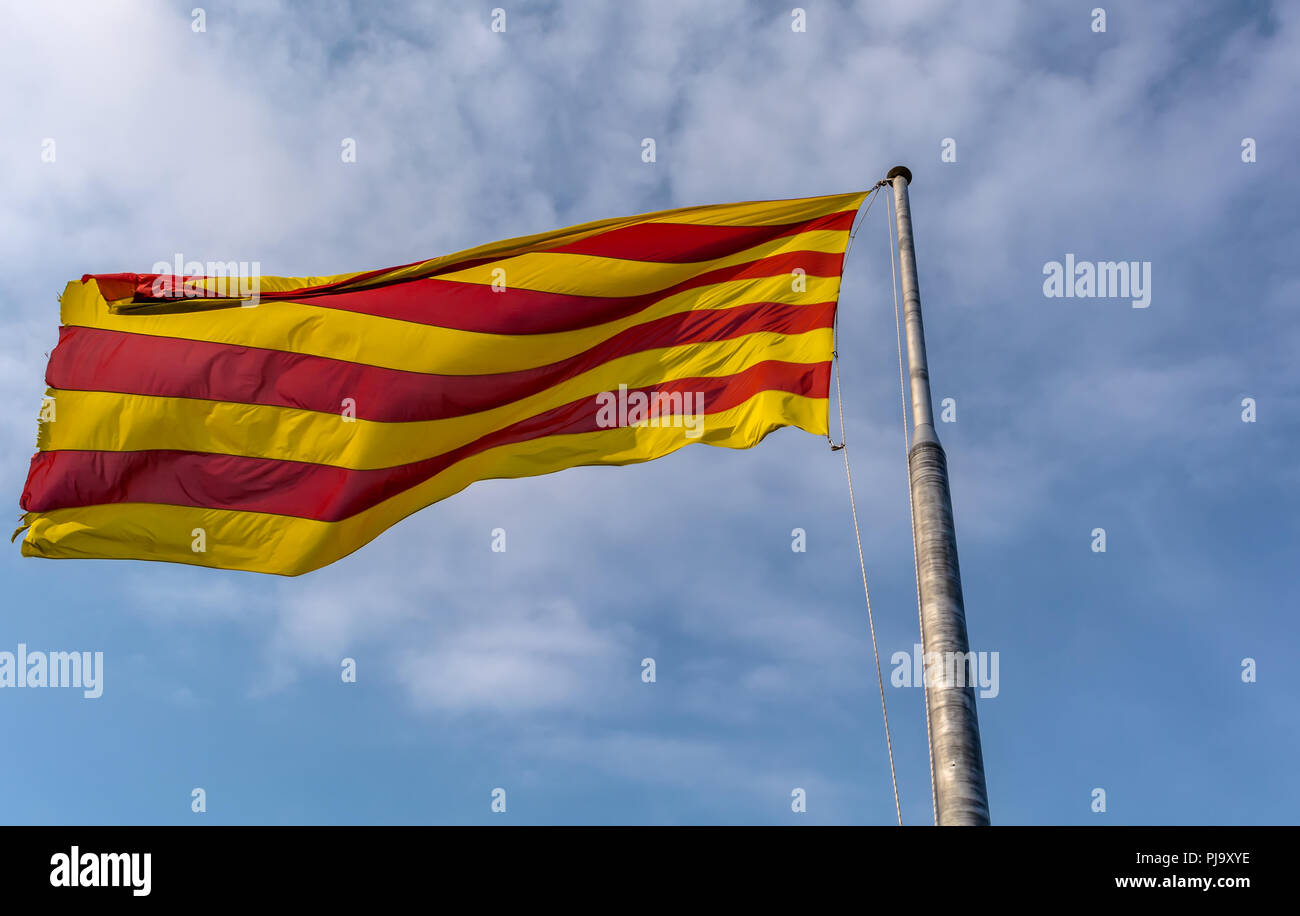 Flag of Catalonia waving in the breeze against blue sky. The flag is ...