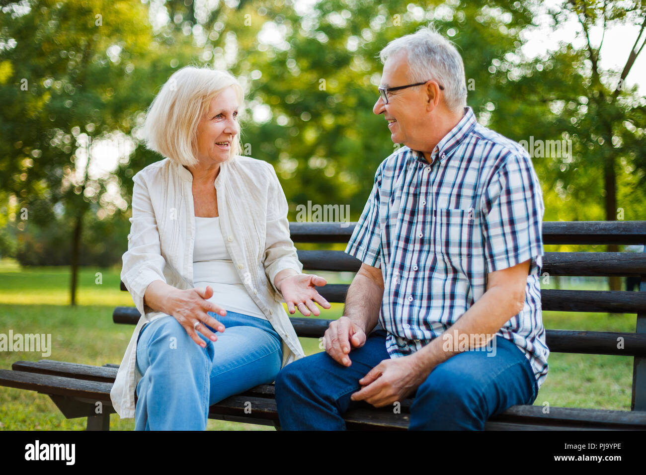 Two happy seniors are sitting and talking in park Stock Photo - Alamy