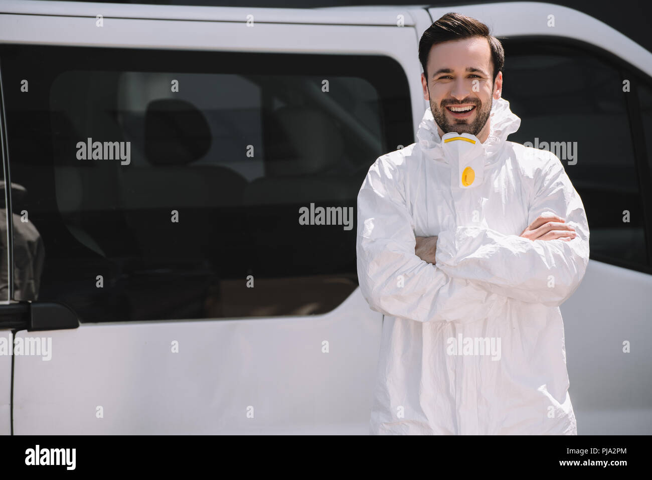 happy pest control worker in uniform standing with crossed arms near ...