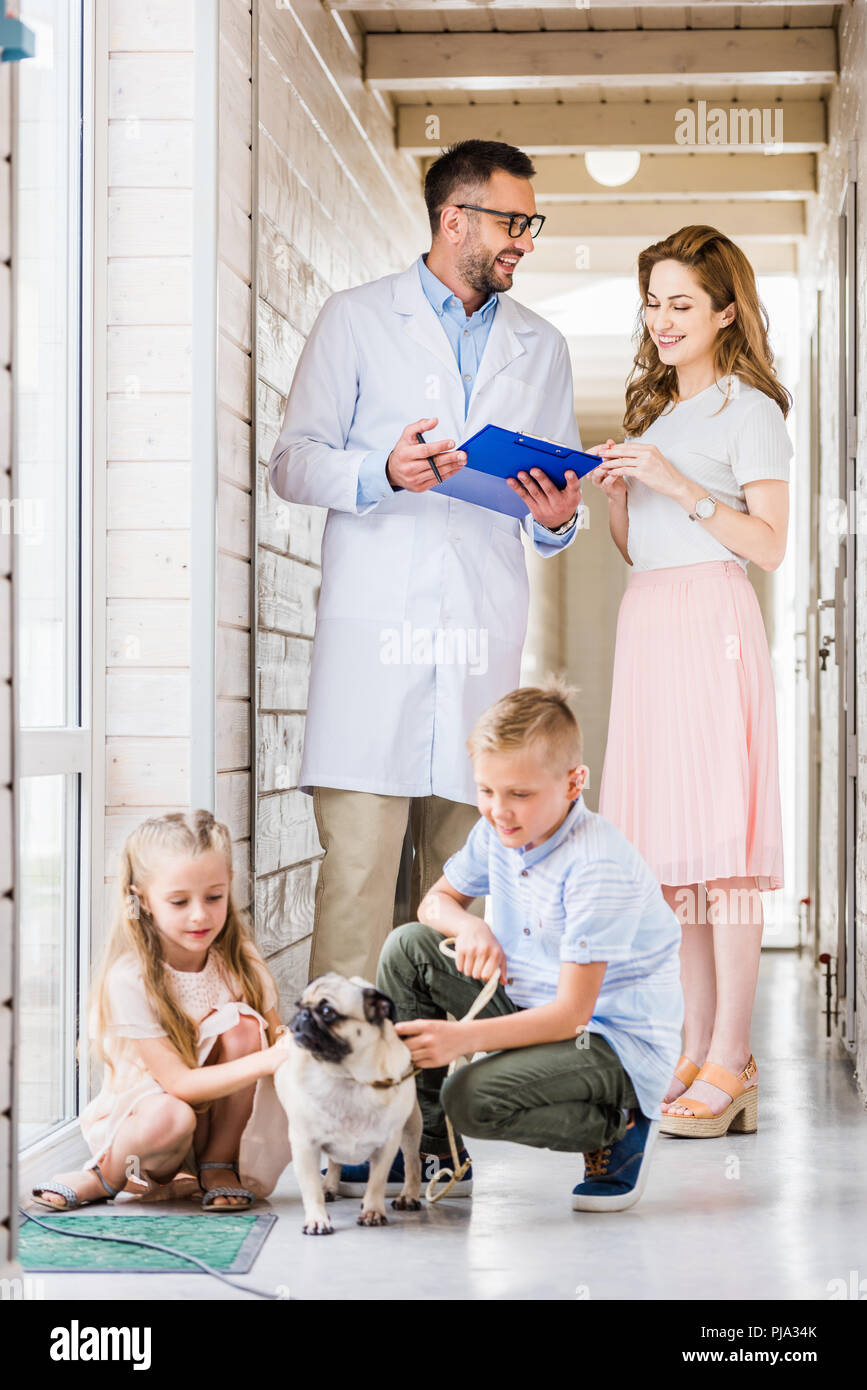 veterinarian showing something in clipboard to woman, kids playing with ...