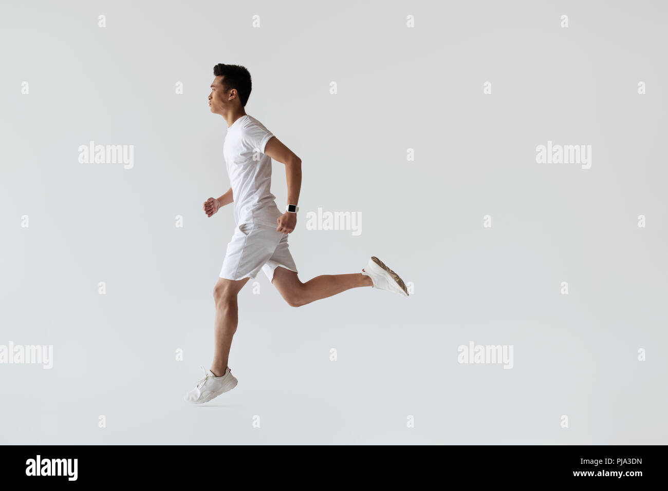 side view of young asian jogger running on grey background Stock Photo ...