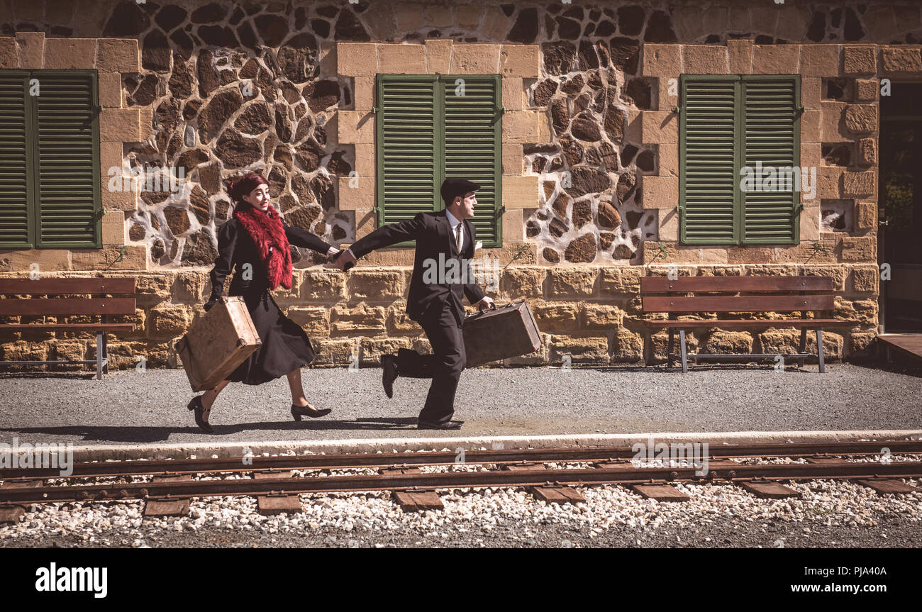 Young couple with vintage suitcase running fast outside a train station ...