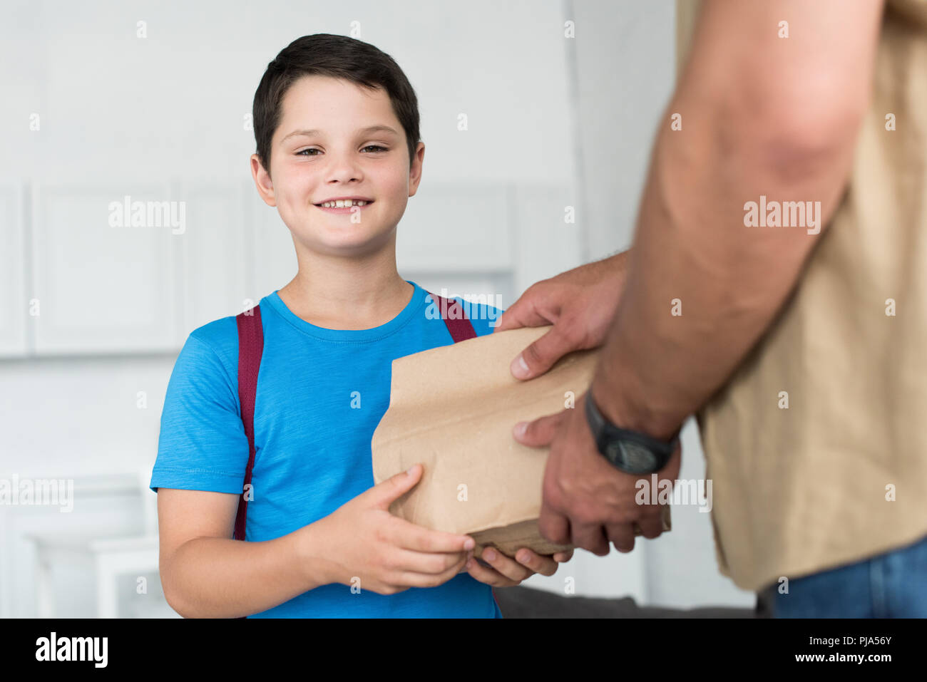 partial view of father giving paper package with food to smiling son ...