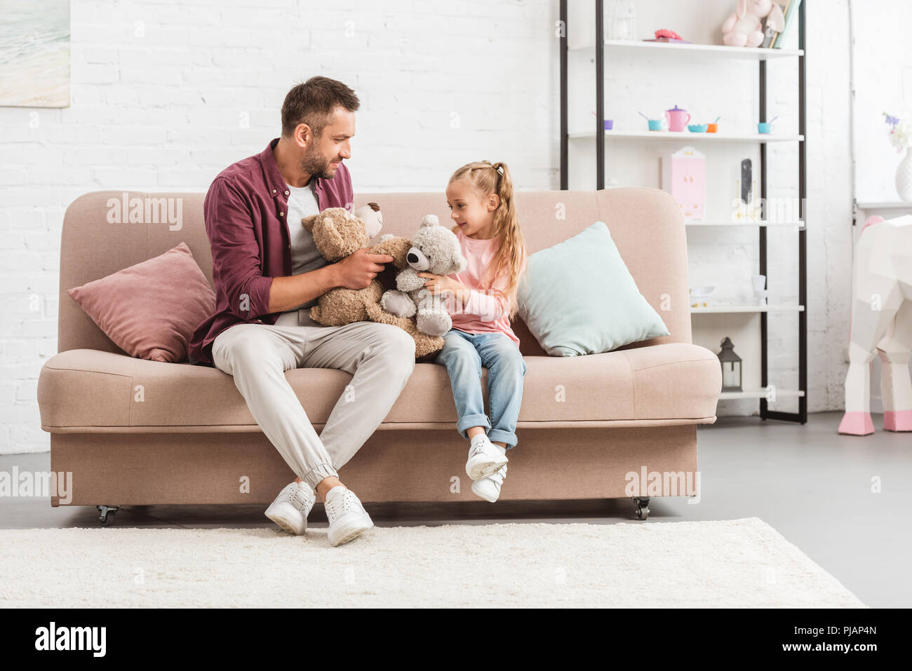 father and daughter playing with teddy bears, sitting on couch and ...