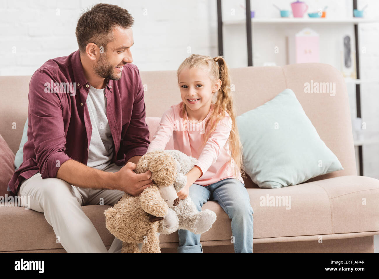 father and smiling daughter holding teddy bears, sitting on couch Stock ...