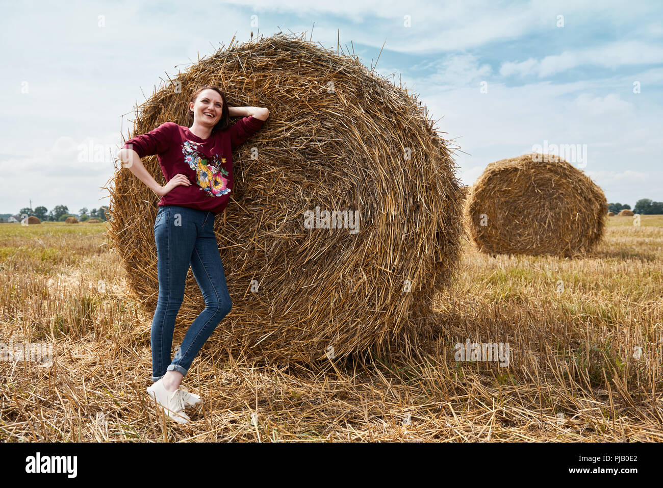 young girl having fun in the field, mowed hay wrapped in a haystack ...