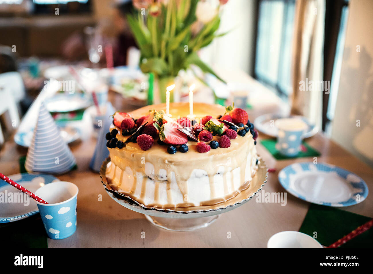 A birthday cake on a glass stand and a vase with tulips on the table ...