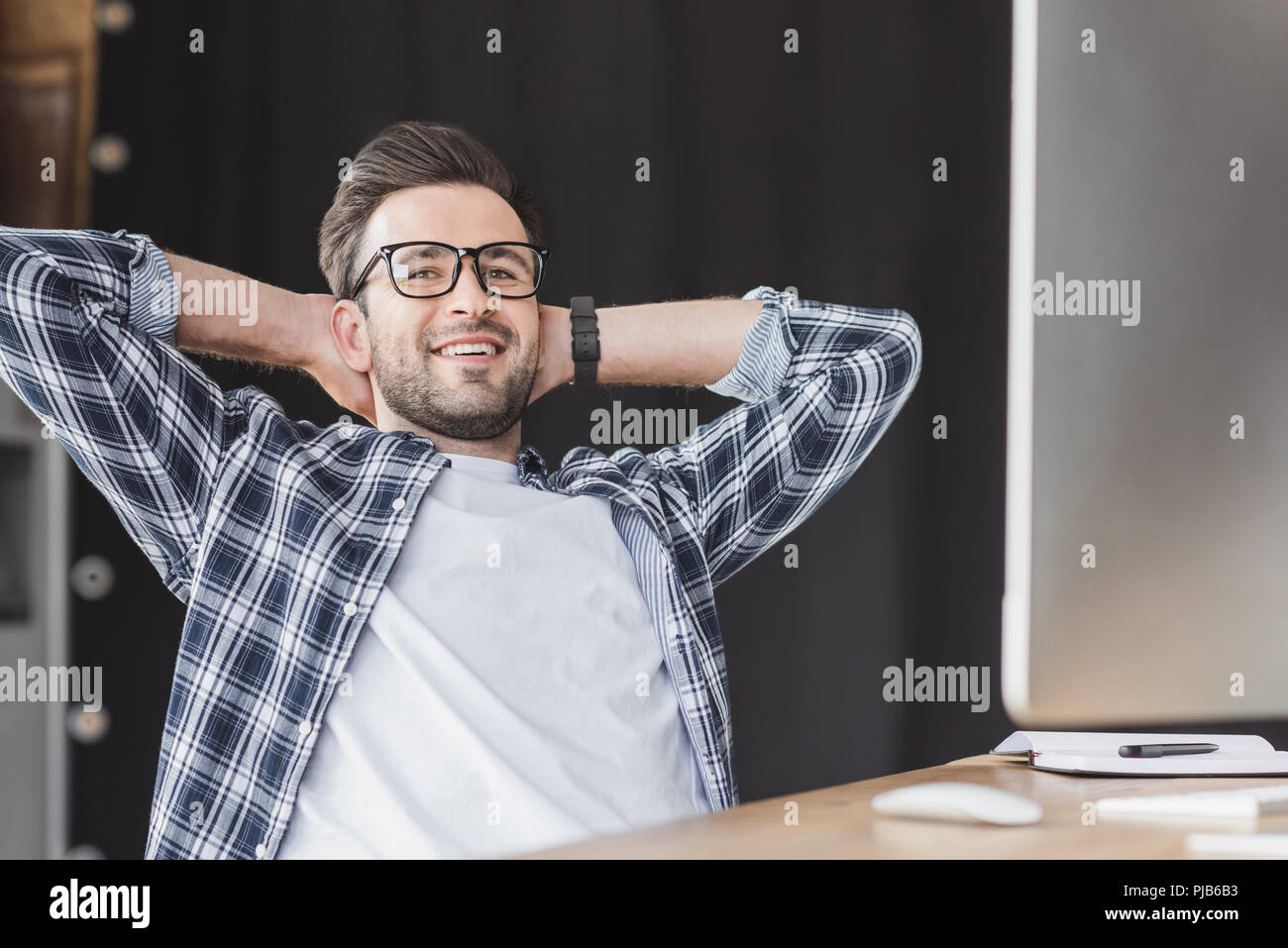 handsome young programmer in eyeglasses smiling at camera while sitting ...