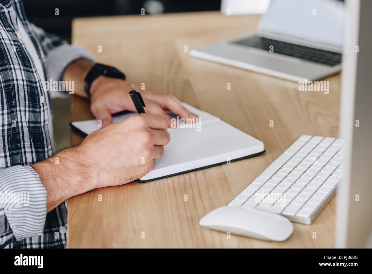 cropped shot of man taking notes in notepad while using desktop ...