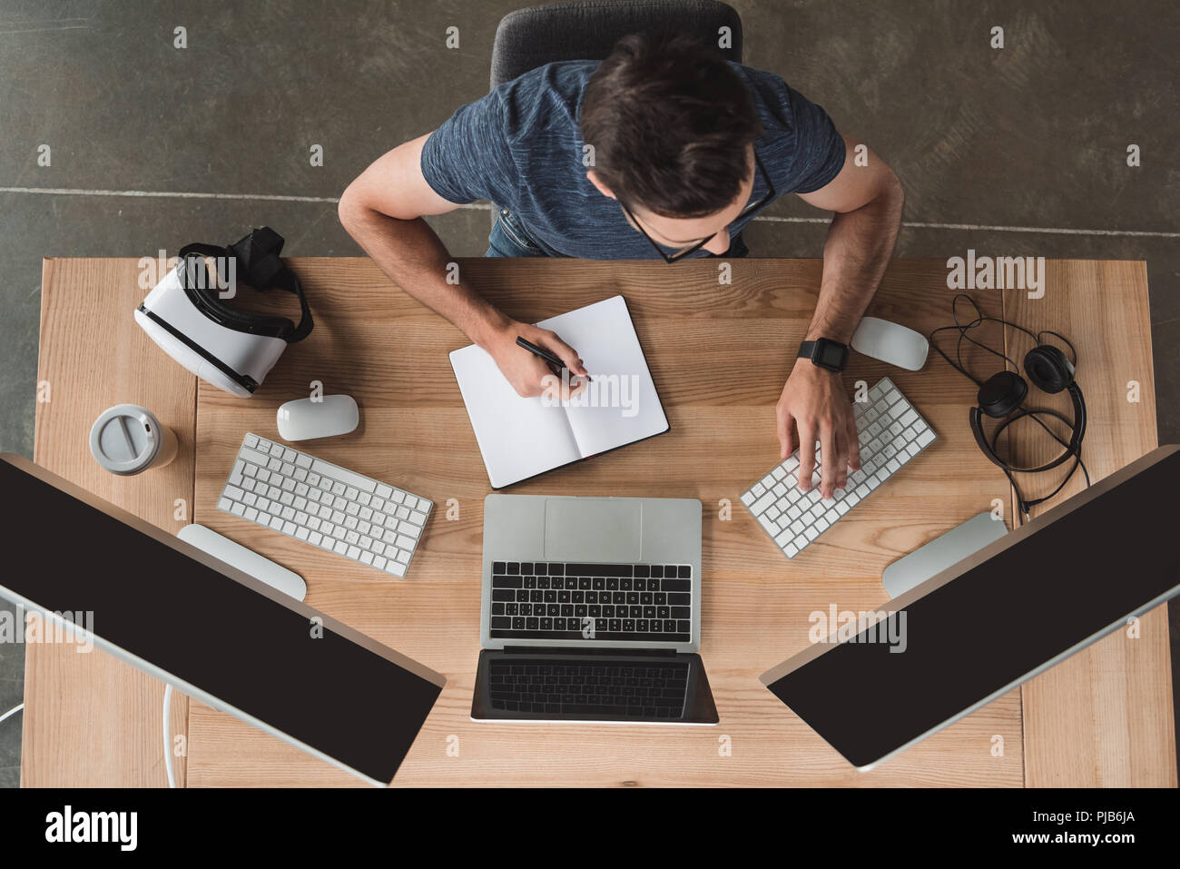 overhead view of young programmer taking notes in notebook and using ...