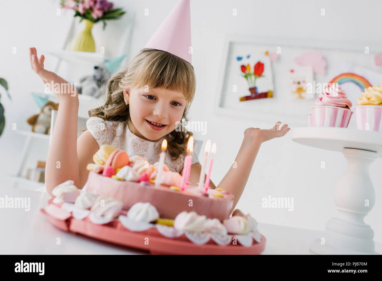 smiling little child with wide arms looking at birthday cake with ...