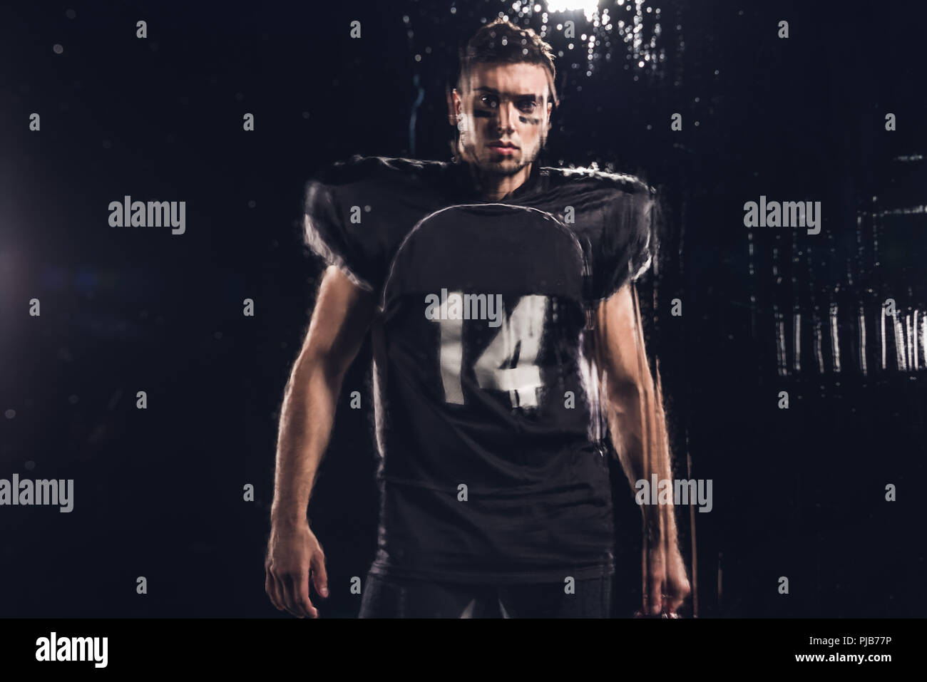 view of young american football player looking at camera on black ...