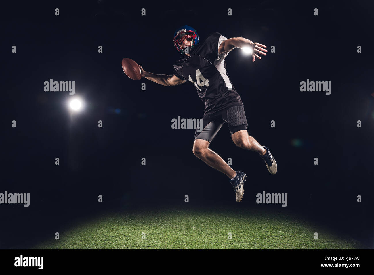 american football player jumping with ball under spotlights on black ...