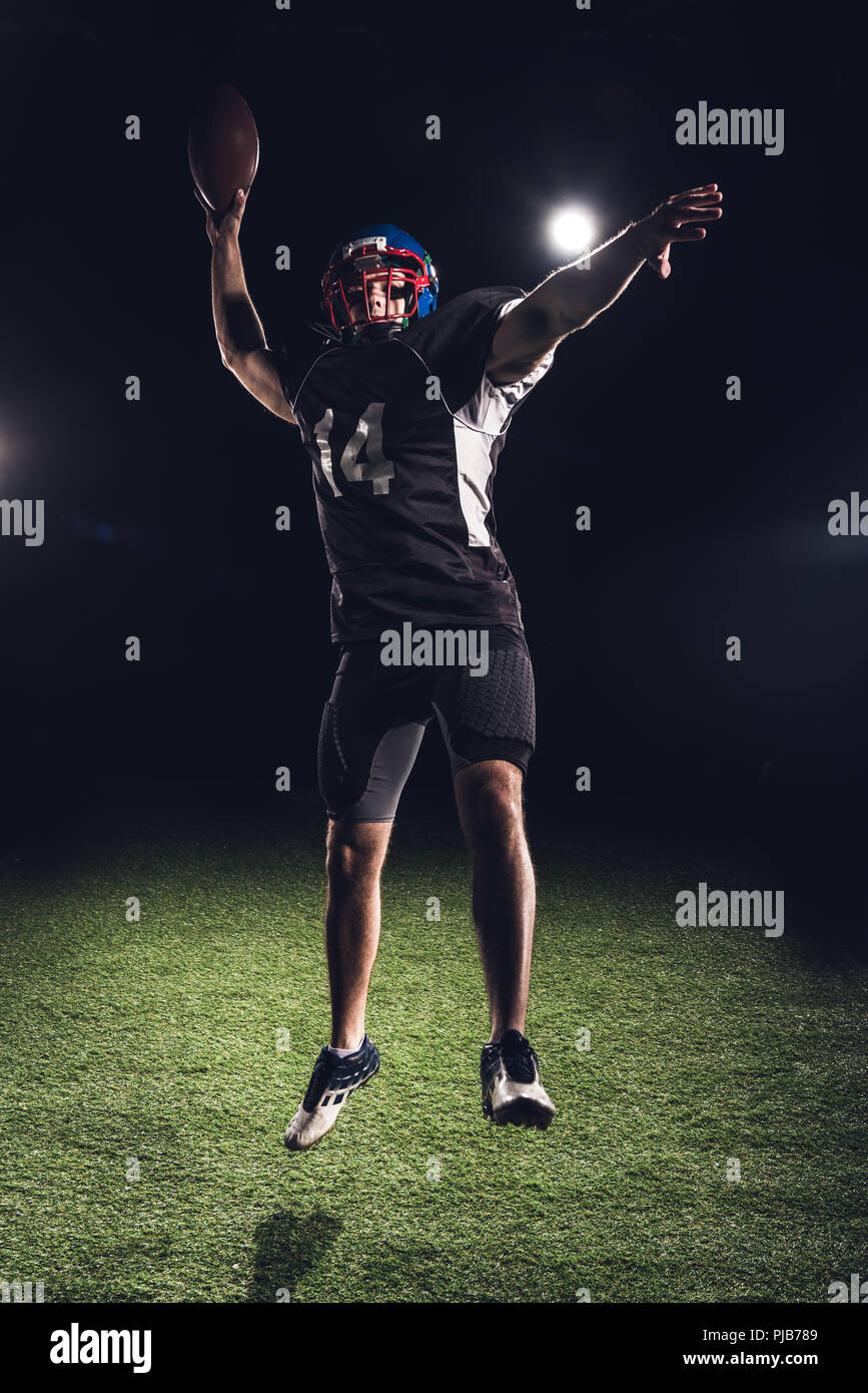 athletic american football player jumping with ball under spotlights on ...