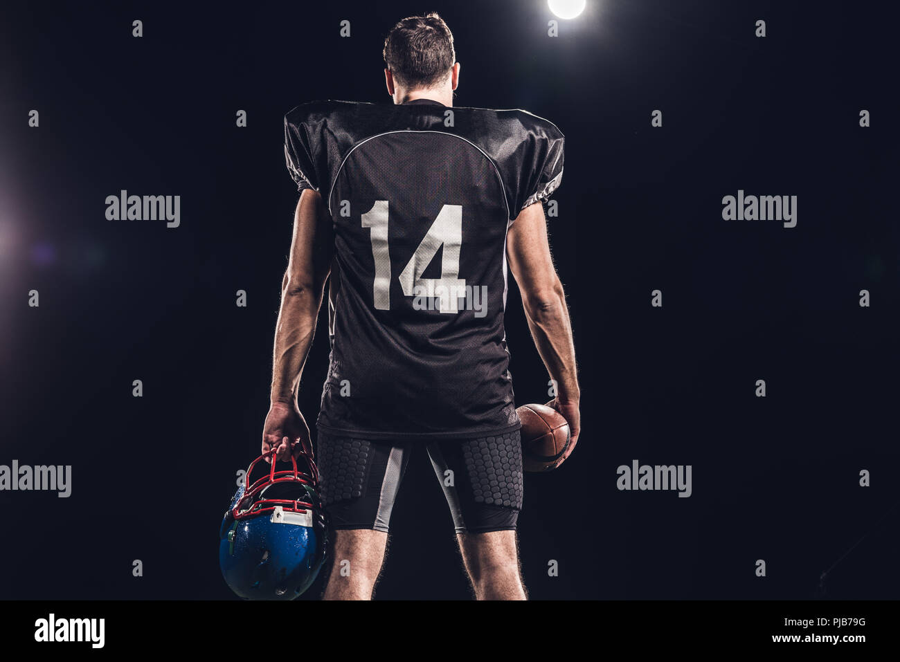 rear view of american football player with ball and helmet under ...