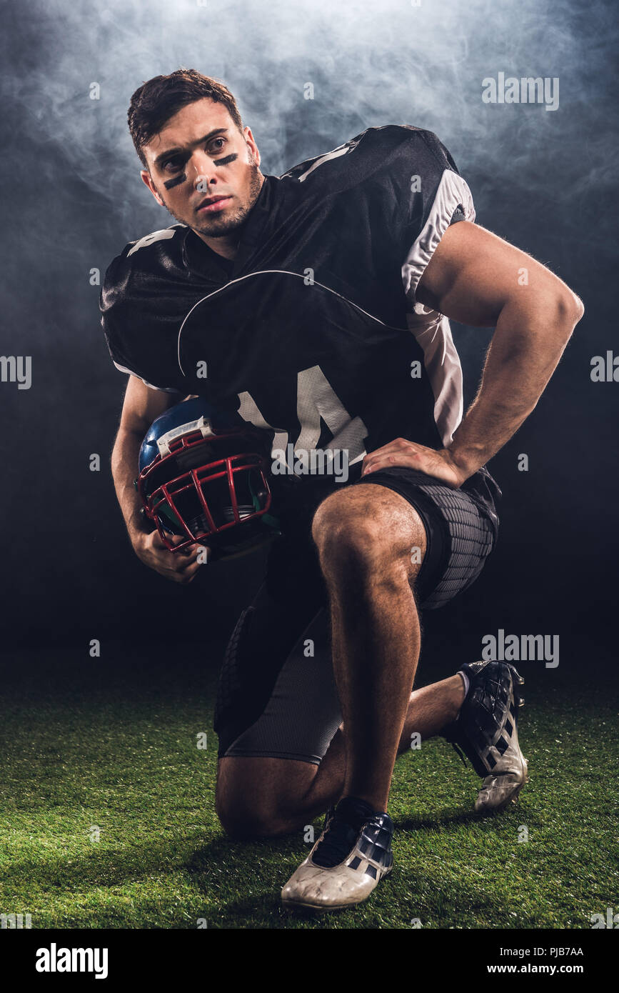 attractive young american football player with helmet standing on knee ...