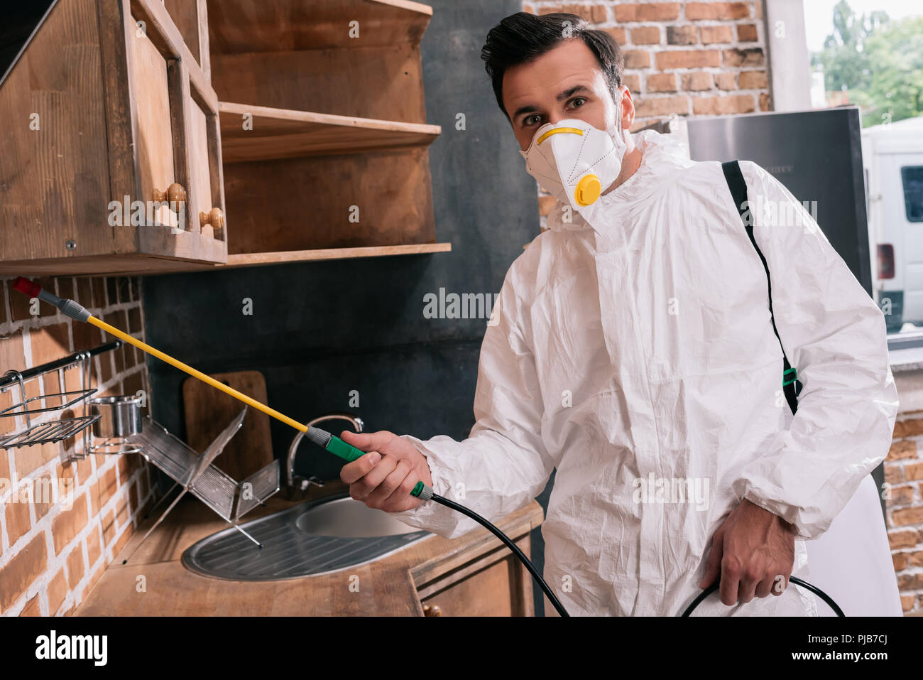 pest control worker spraying pesticides under shelves in kitchen and ...