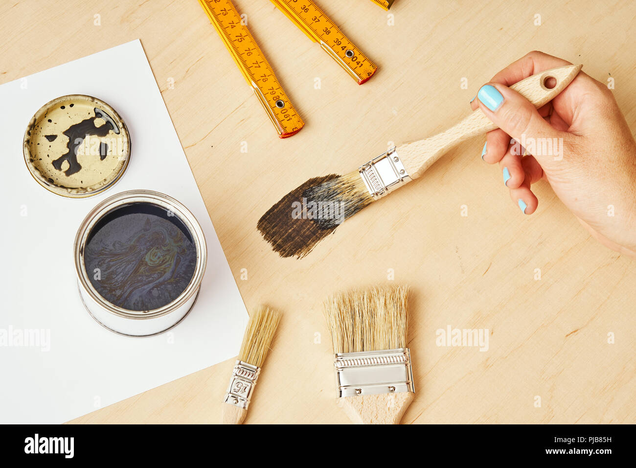 woman's hand is holding a brush with paint and painting a wooden table ...