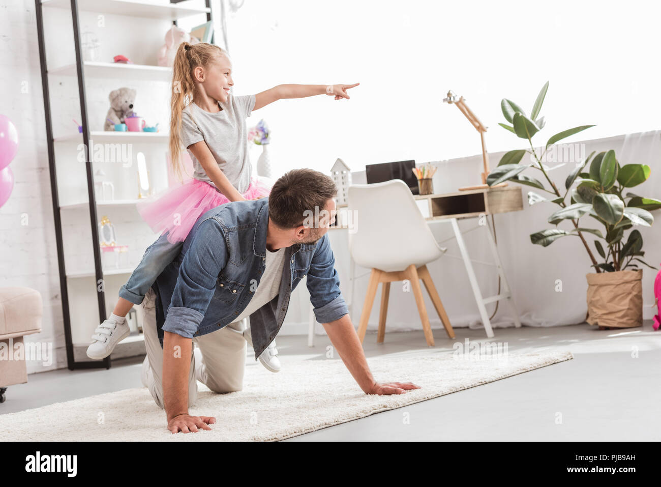 daughter sitting on on father back and showing something in window ...
