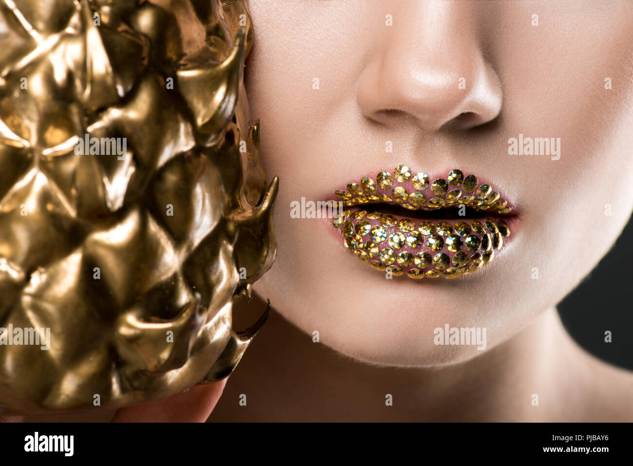 cropped view of woman with gild lips holding golden pineapple Stock ...