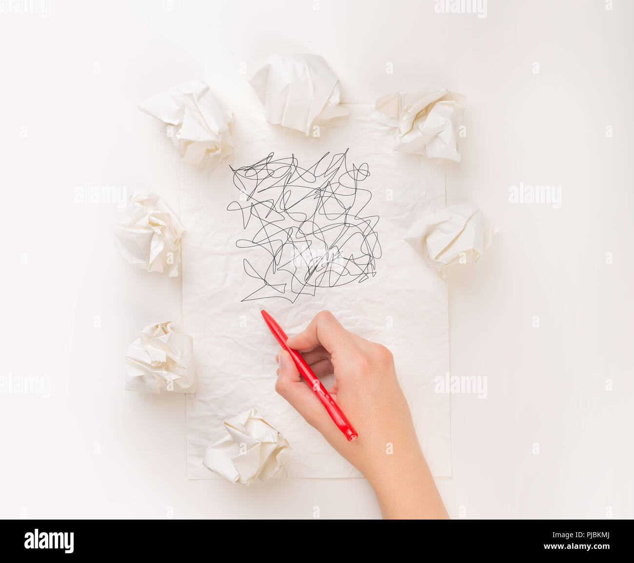 Female hand next to a few crumpled paper balls drawing random scribbles ...