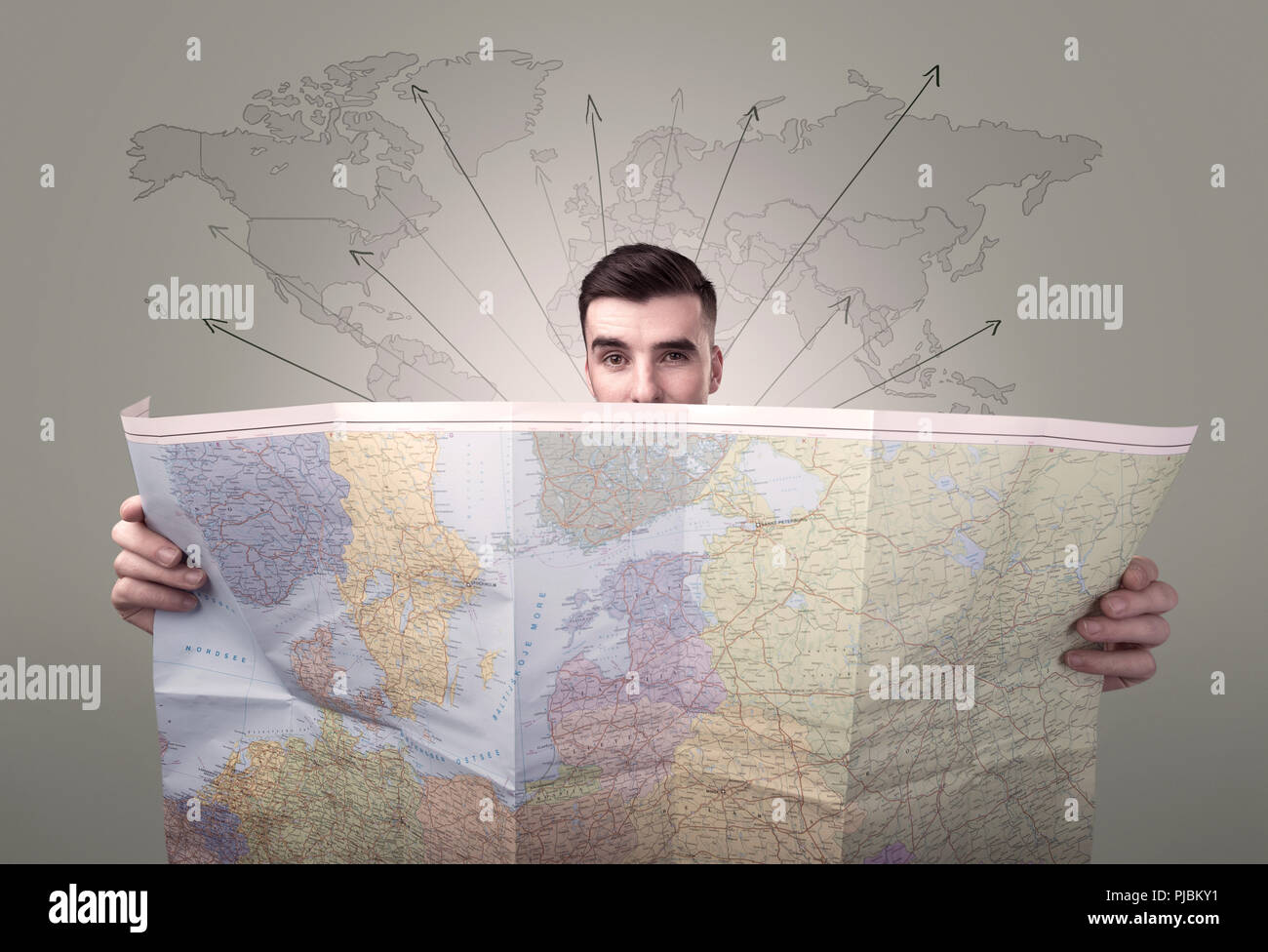 Handsome young man holding a map with world map and arrows behind him ...
