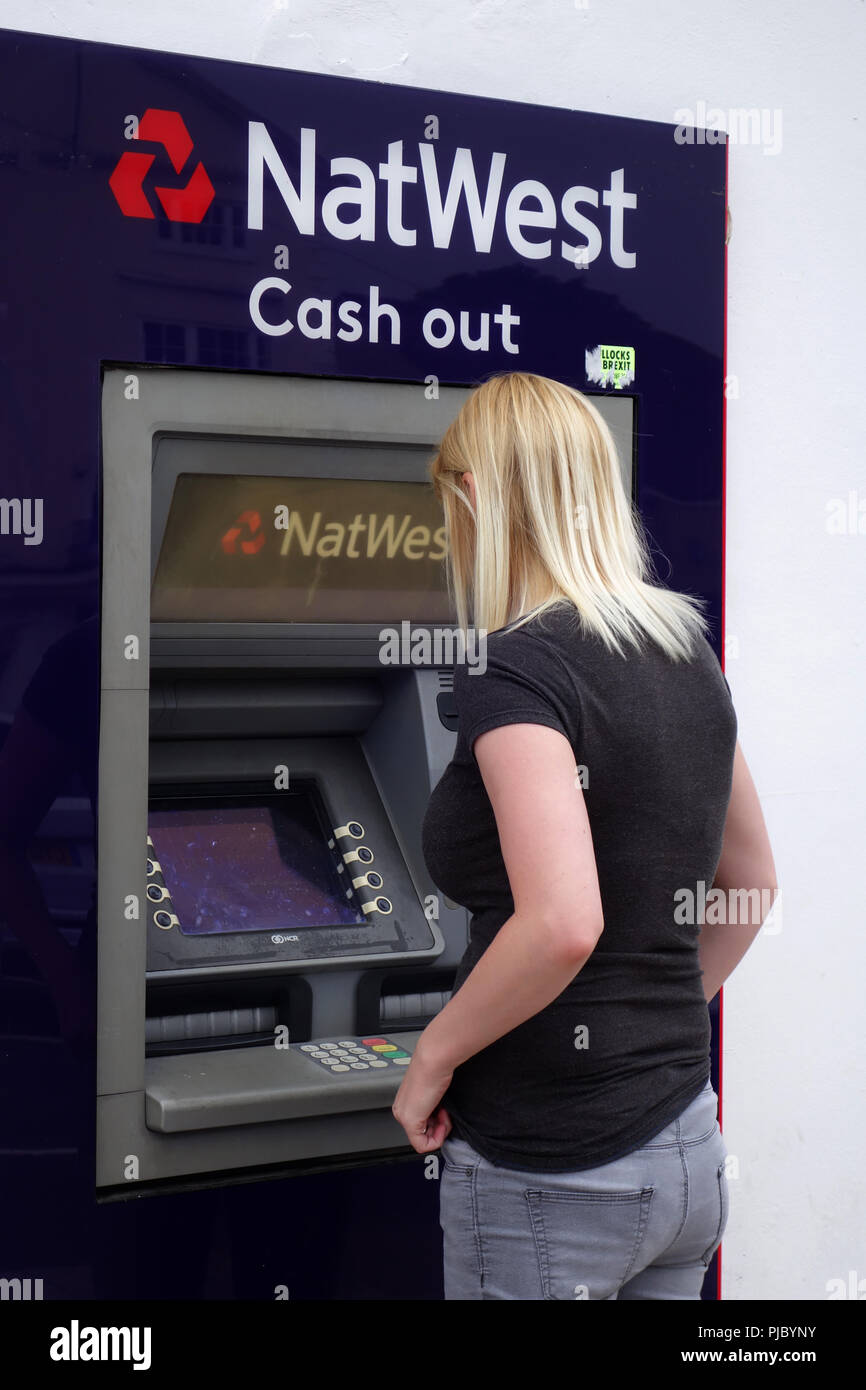 back view of a Young woman using a Nat West ATM in the village of ...