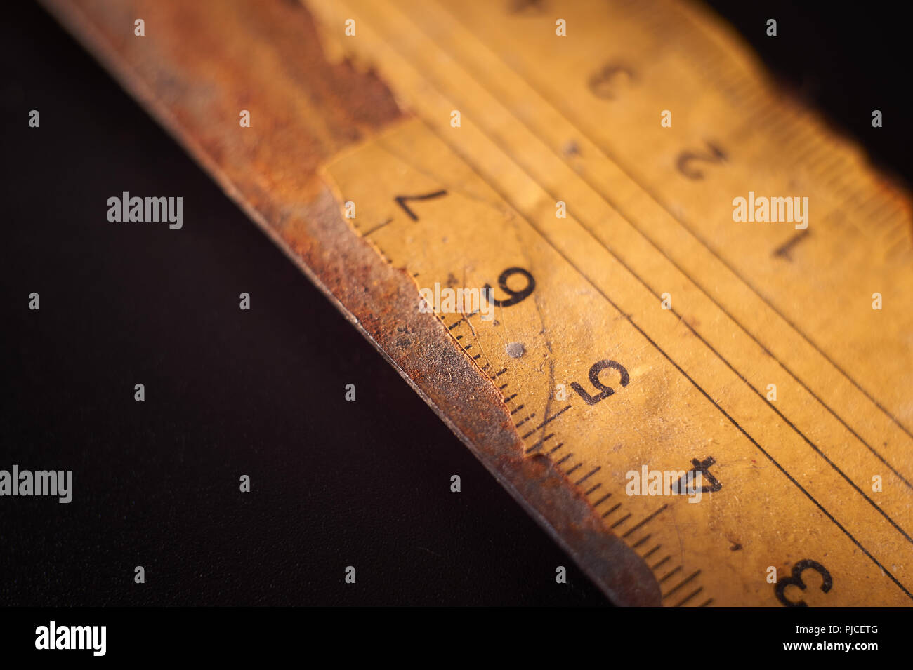 Old rusty metal ruler with numbered label cracking on black background ...