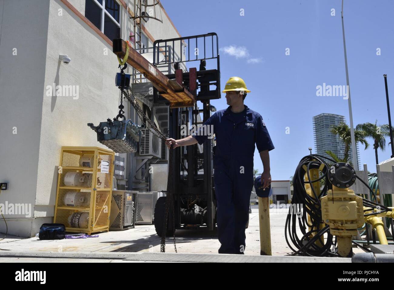 A Coast Guard engineer guides a crane carrying an engine head to a ...