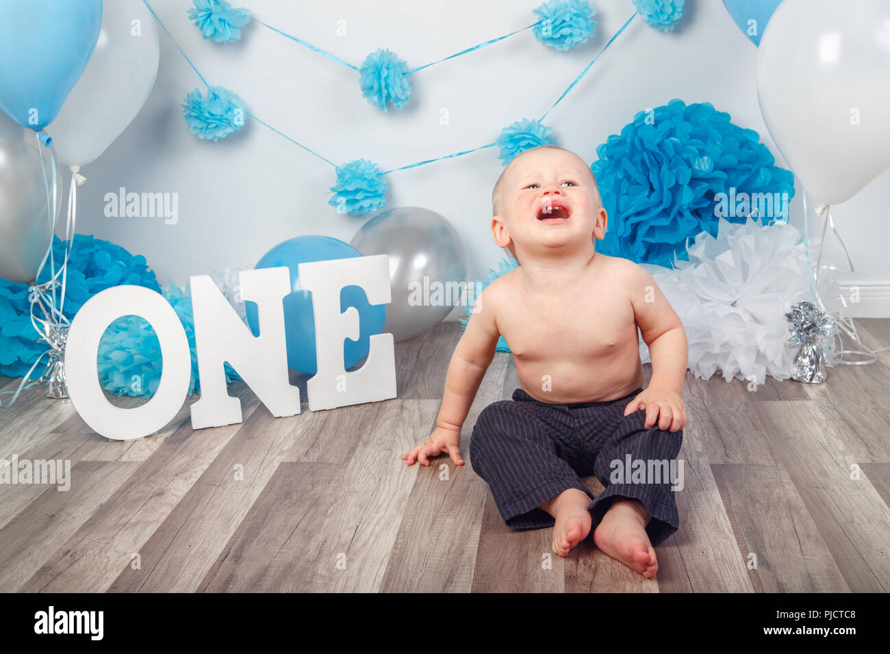 Portrait of crying screaming unhappy Caucasian baby boy in dark pants ...