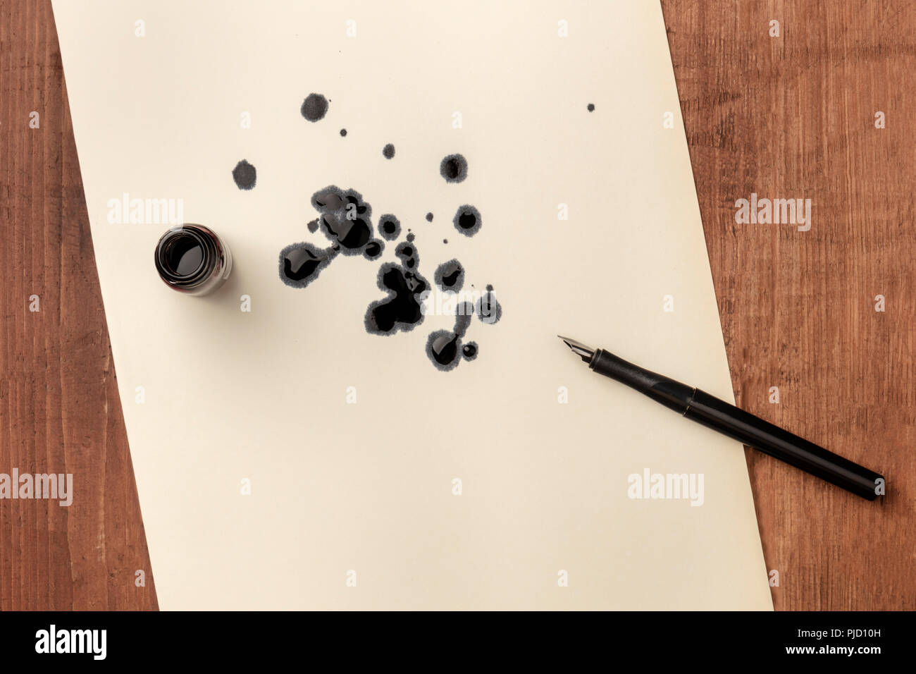 An overhead photo of an ink well with drops of ink on paper, with a nib ...