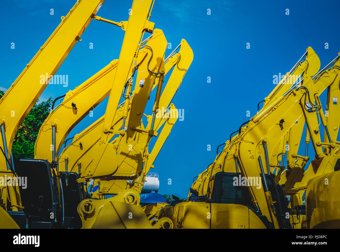 Yellow backhoe with hydraulic piston arm against clear blue sky. Heavy ...
