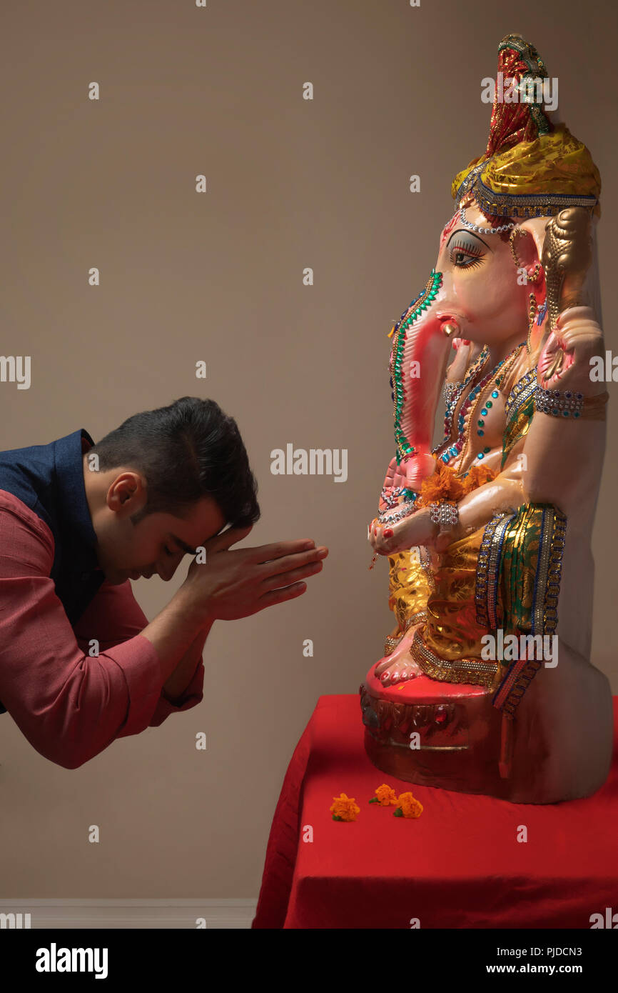 Man praying with hands joined and eyes closed in front of Ganpati Idol ...