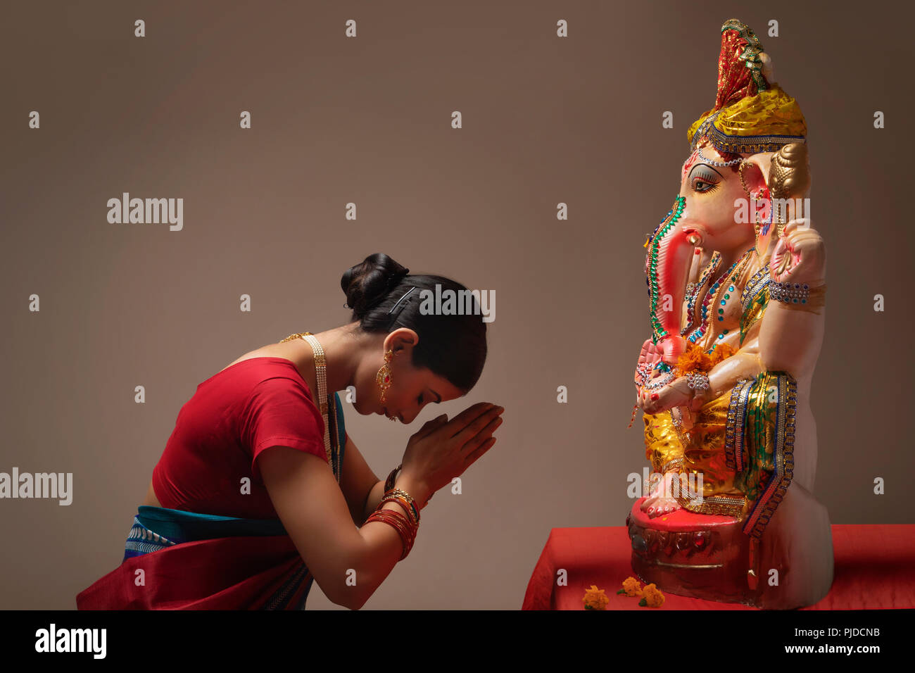 Woman praying with hands joined and eyes closed in front of Ganpati ...