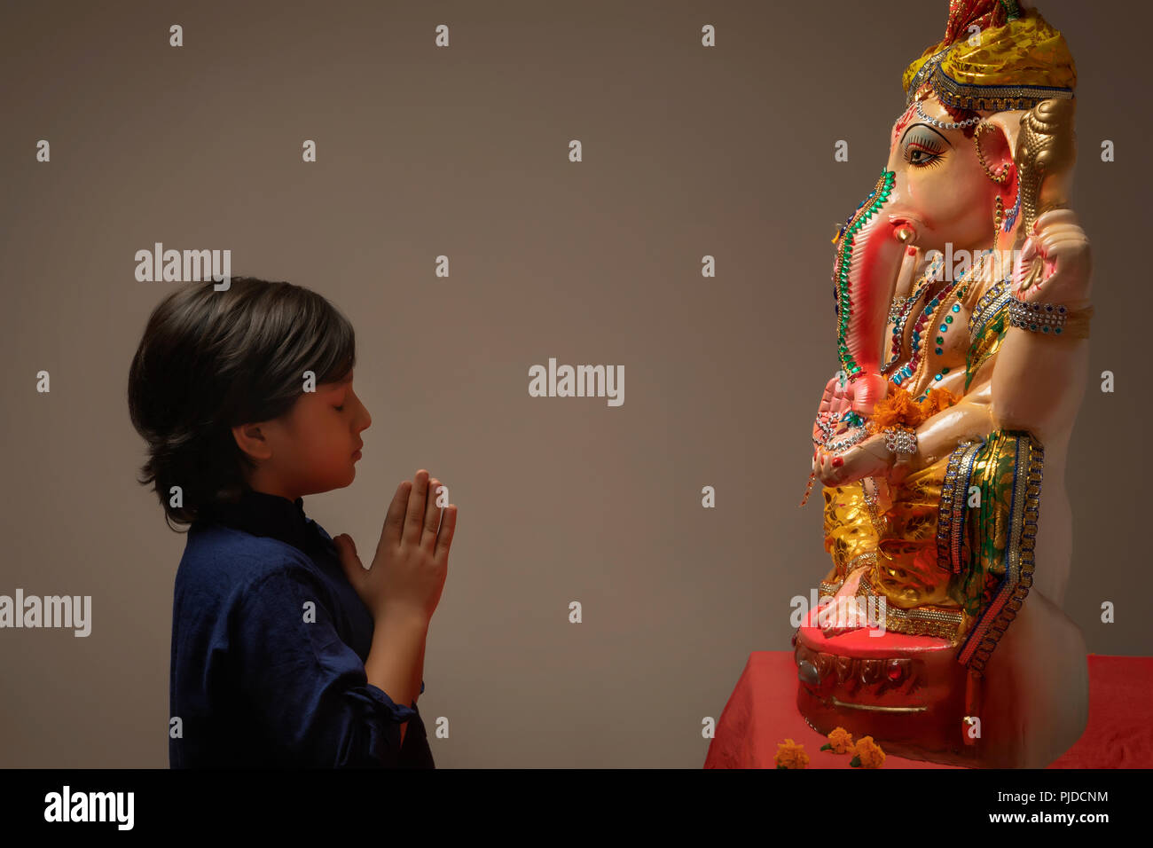 Kid praying with hands joined and eyes closed in front of Ganpati Idol ...