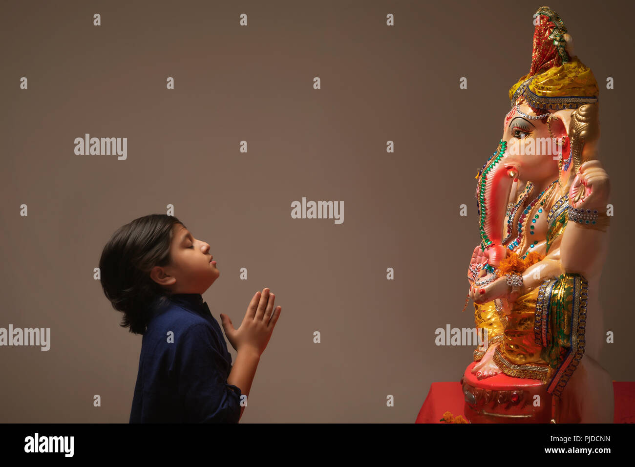 Kid praying with hands joined and eyes closed in front of Ganpati Idol ...